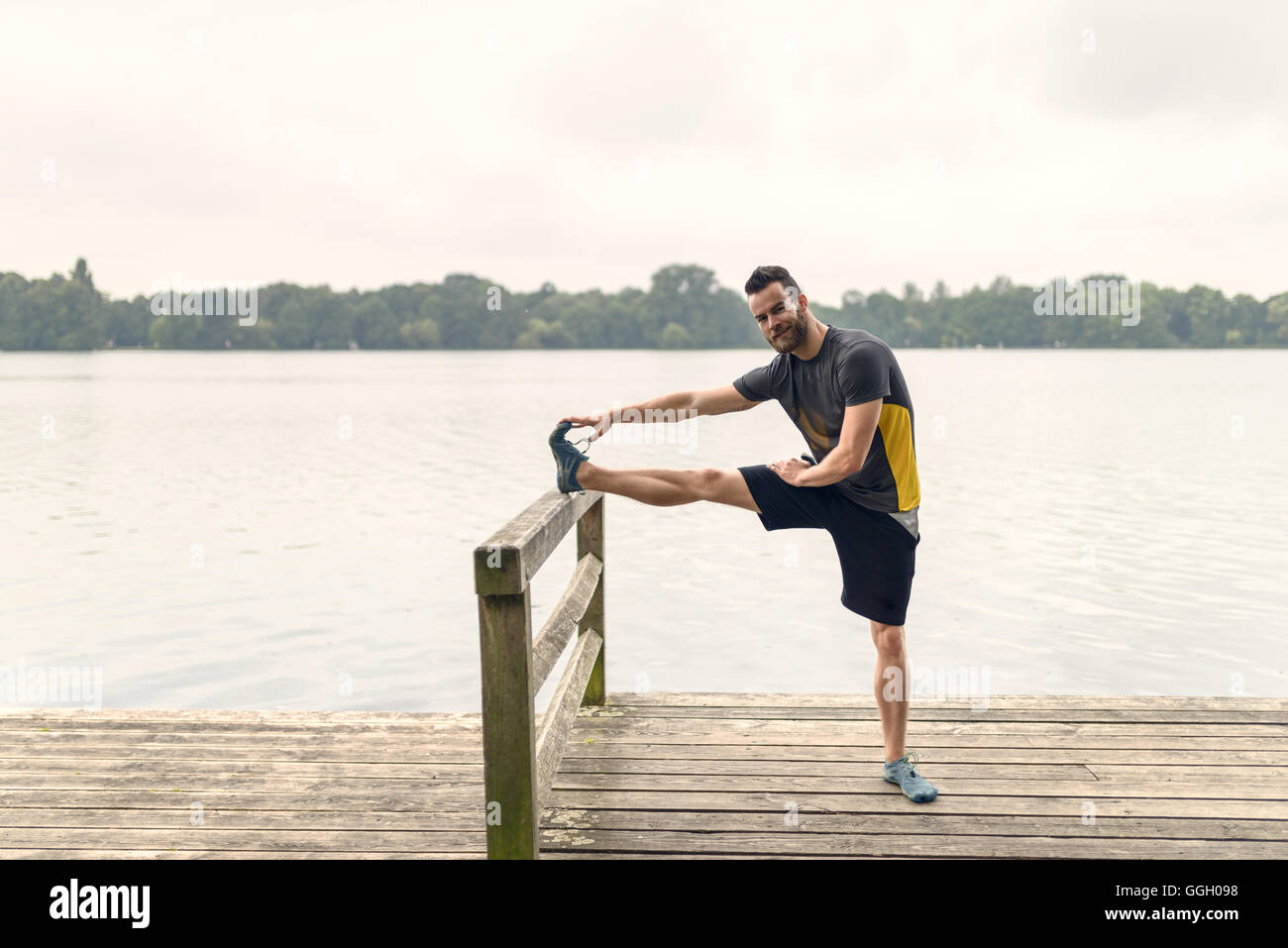 Young man doing stretching exercises on a wooden deck overlooking a ...