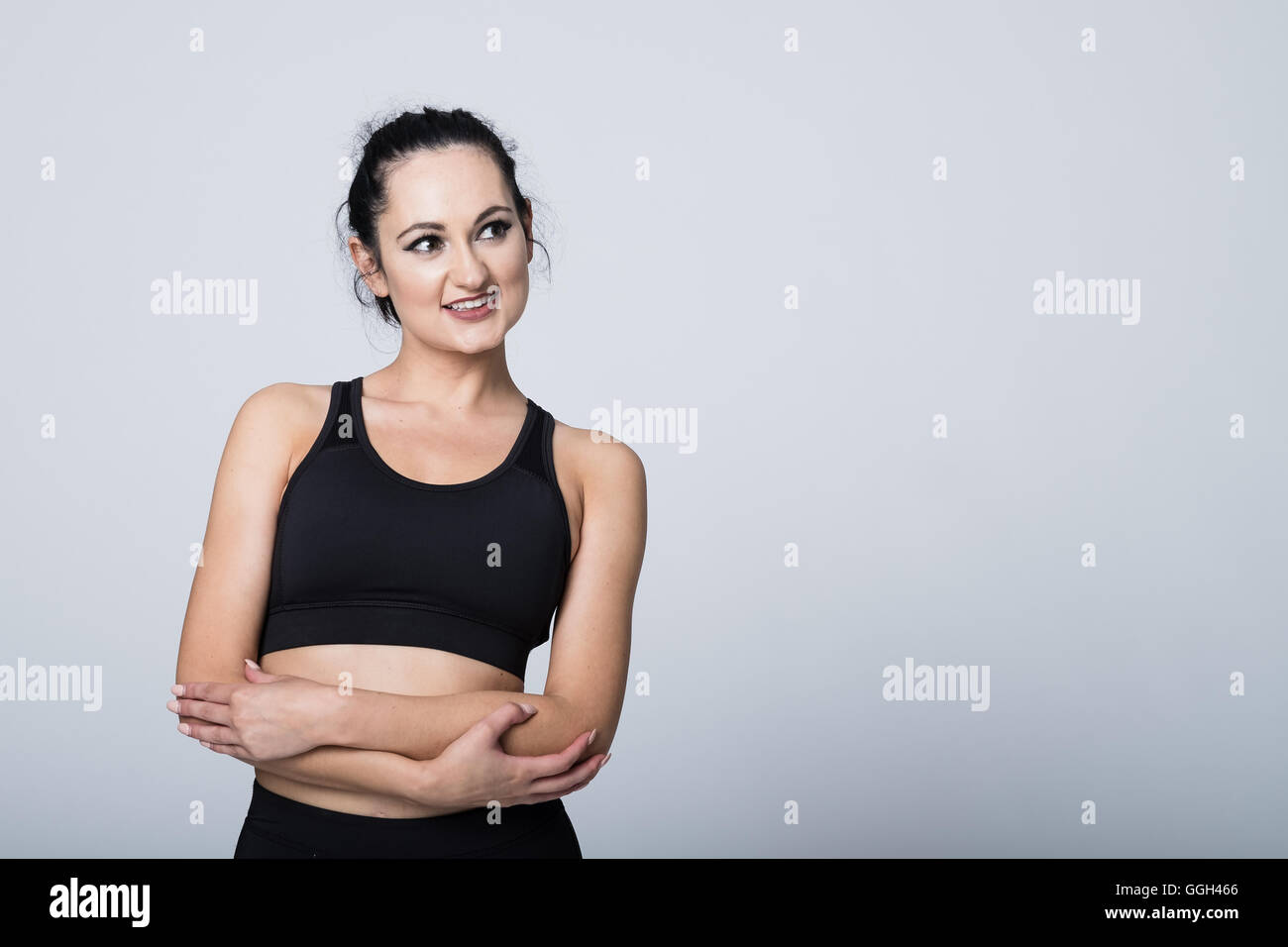 Fit young woman with her arms folded looks up and rightand is smiling ...