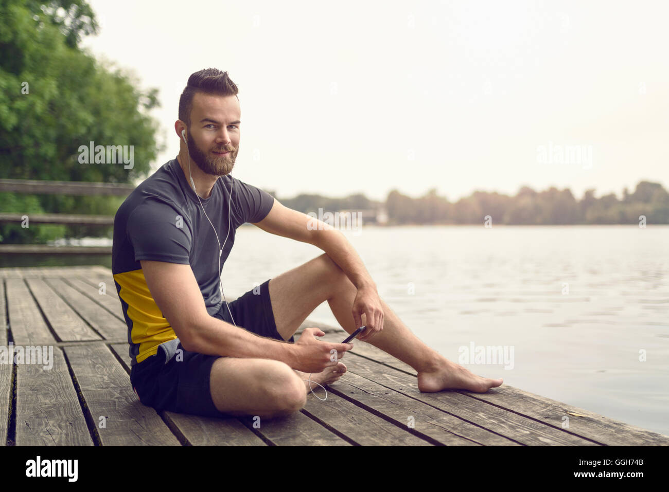 Attractive barefoot bearded young man relaxing on a wooden deck ...