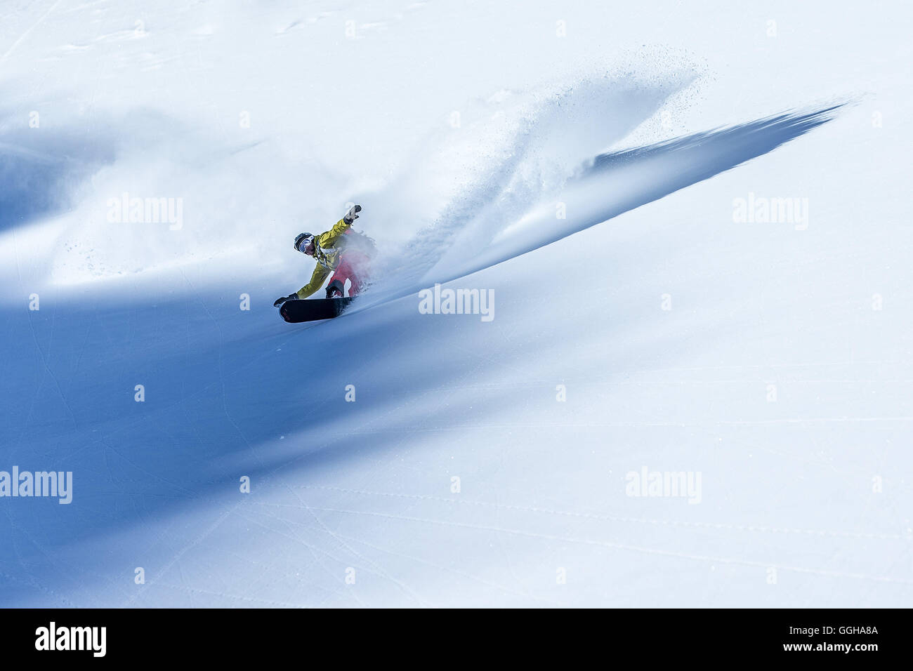 Young male snowboarder riding through deep powder snow in the mountains ...