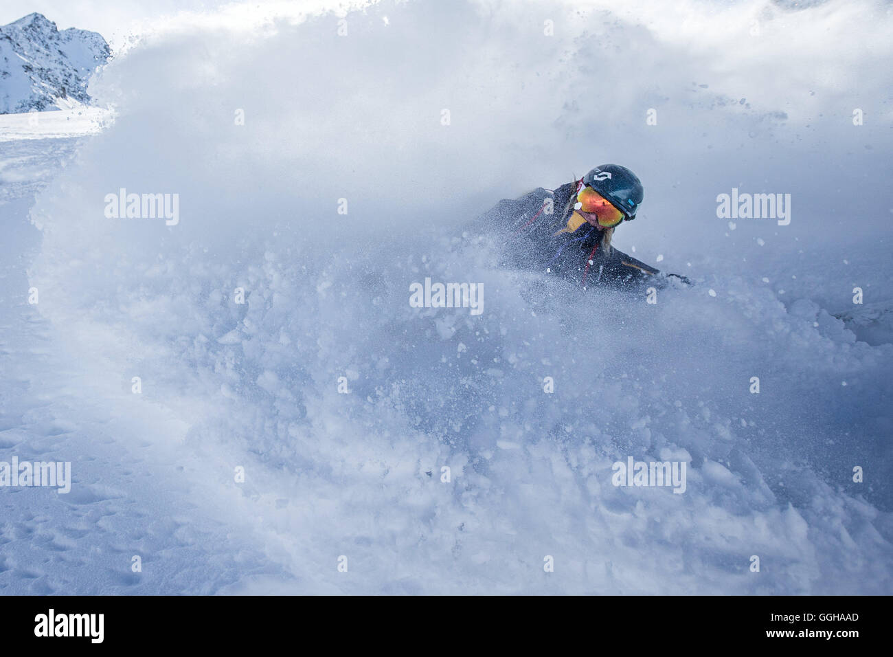 Young female freeskier riding through deep powder snow in the mountains ...