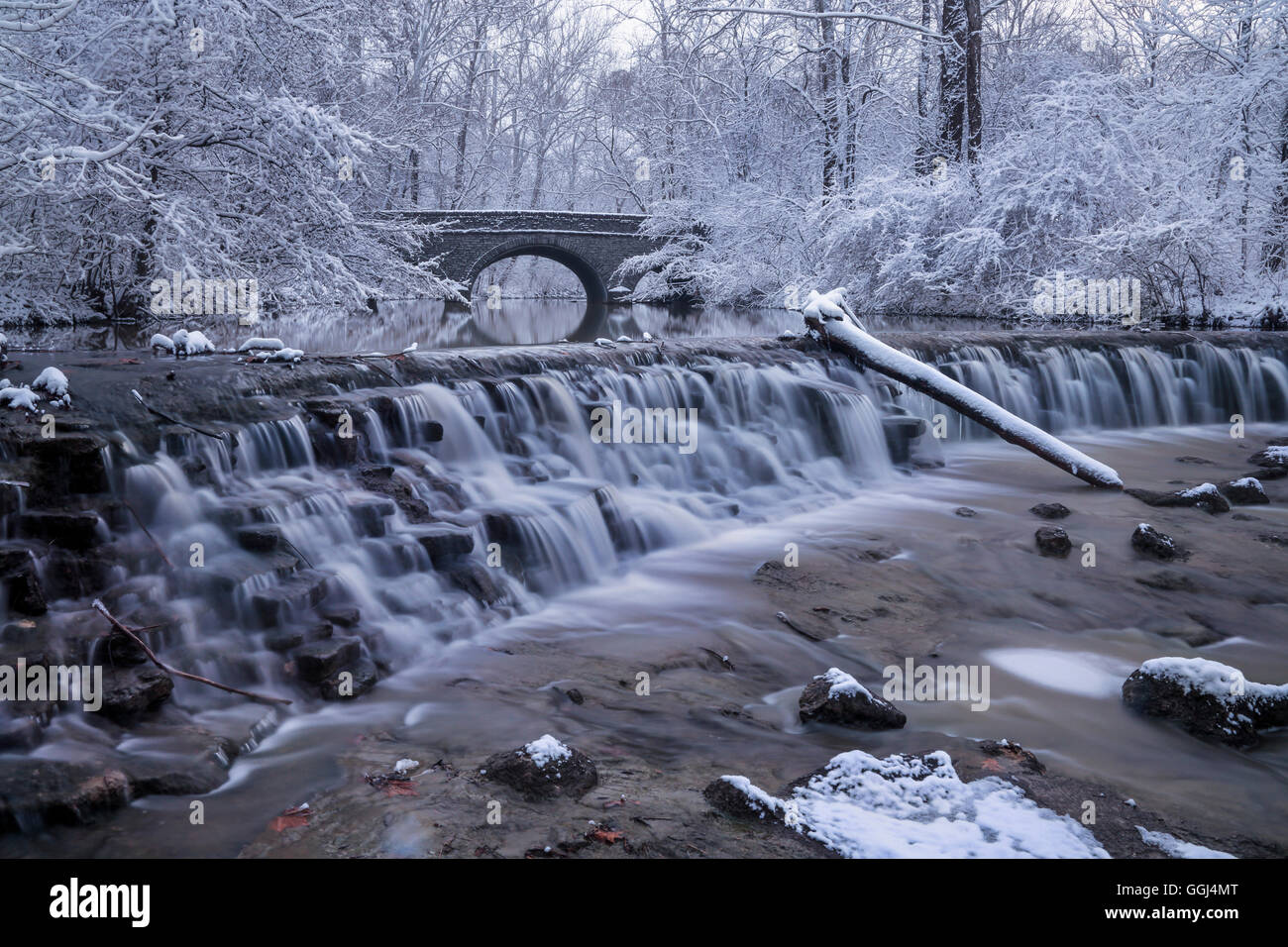 Snow Covered Trees Framing A Stone Bridge And Waterfall During Winter ...