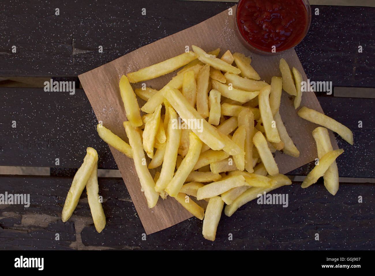 French salted fries in a paper wrapper on rustic background with fresh ...