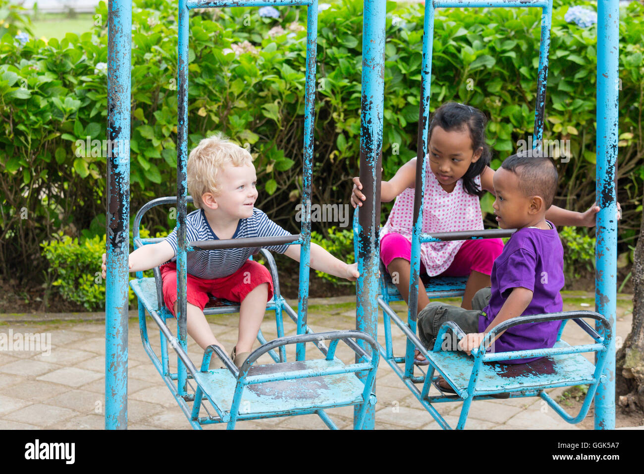 German young boy playing with Balinese kids, on a swing, old blue swing ...