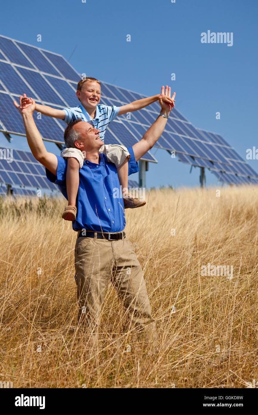 Solar park in summer, man carrying his son on his shoulders and are ...