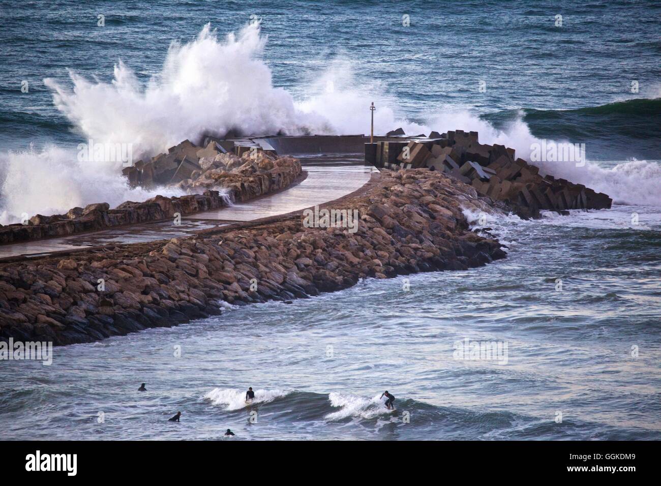 Waves breaking against the port wall of Rabat, with surfers in the ...
