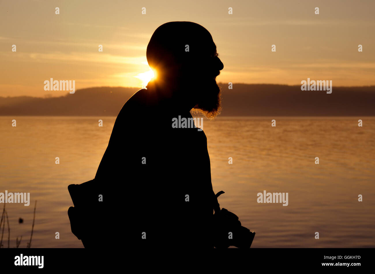 Old man as tourist with camera on Lake Constance at sunset silhouetted ...