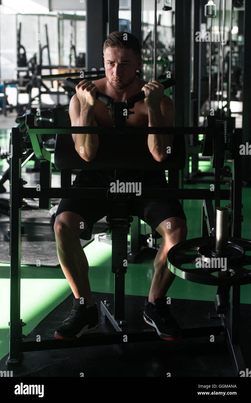 Young Strong Man In The Gym And Exercising Biceps On Machine - Muscular ...