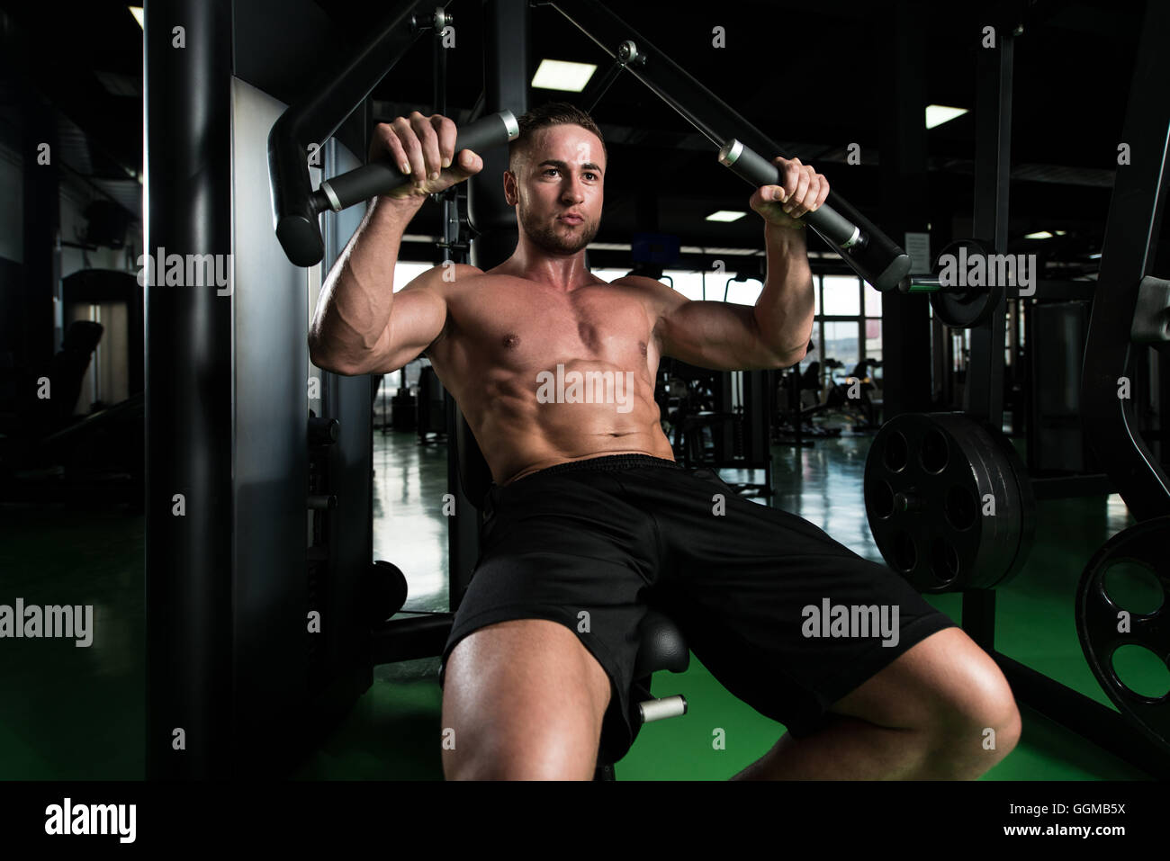 Young Strong Man In The Gym And Exercising Chest On Machine - Muscular ...