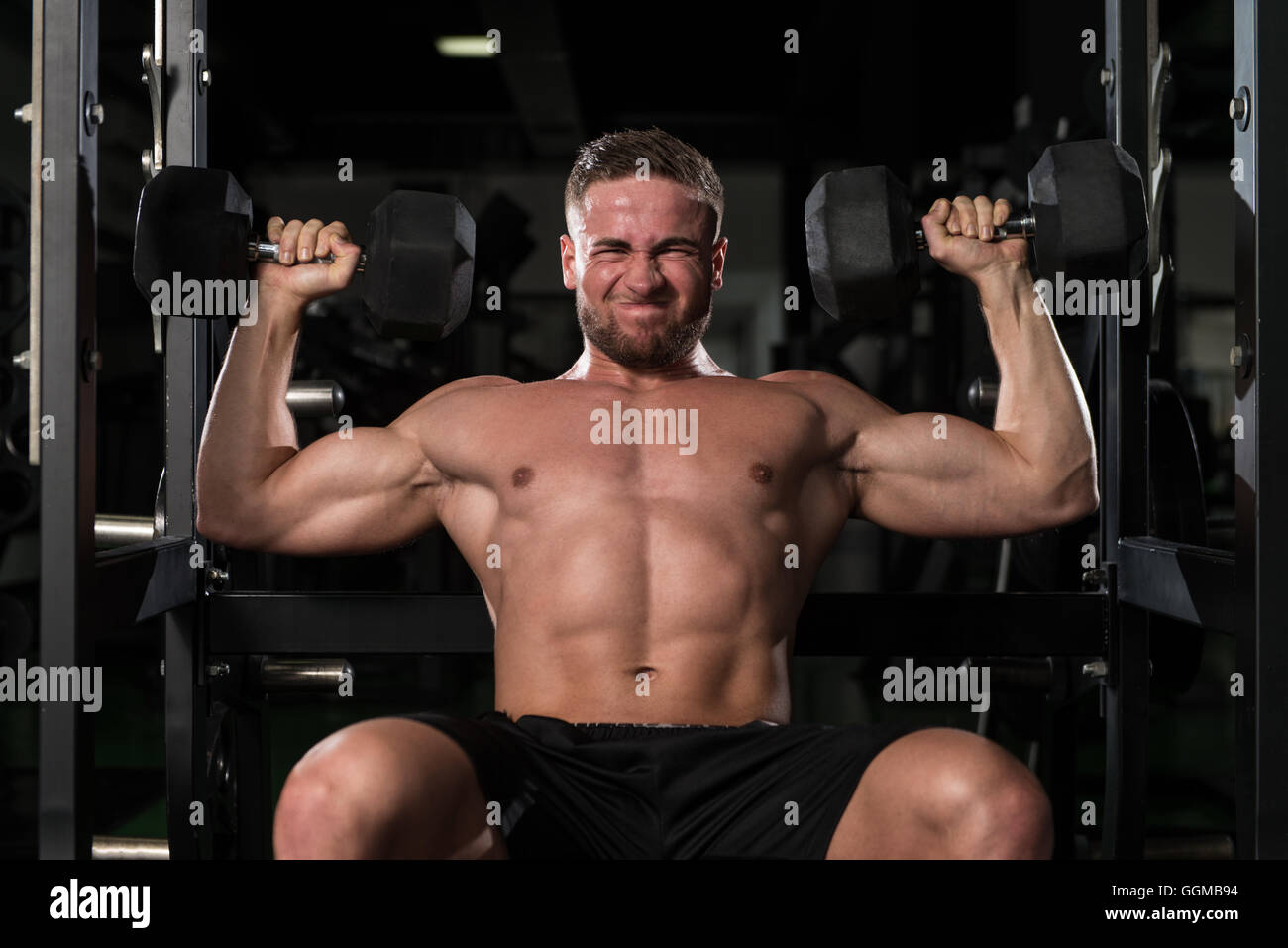Young Man Working Out Shoulders In A Dark Gym - Dumbbell Concentration ...