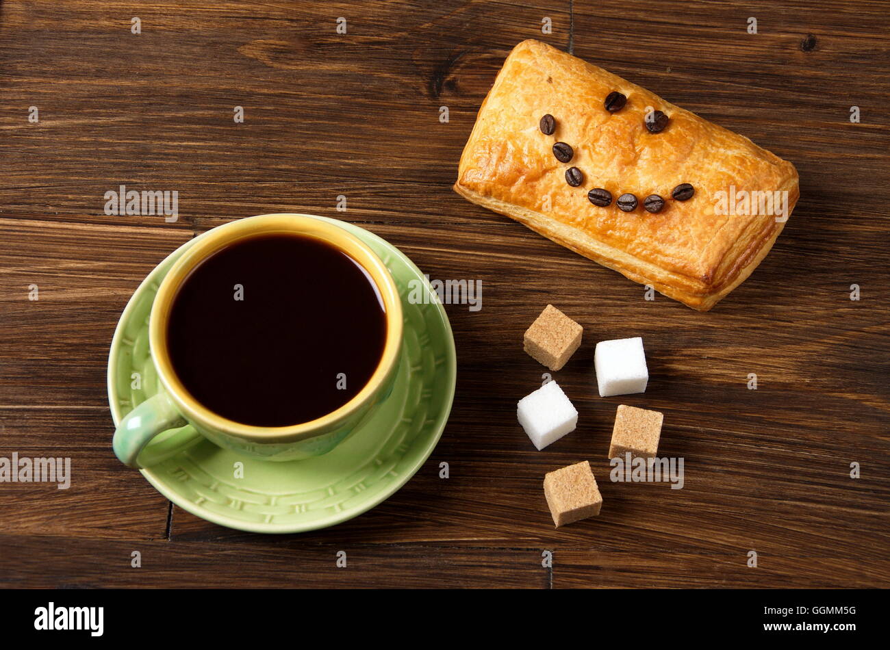 Green cup of coffee near white, brown sugar cubes and puff with a smile ...