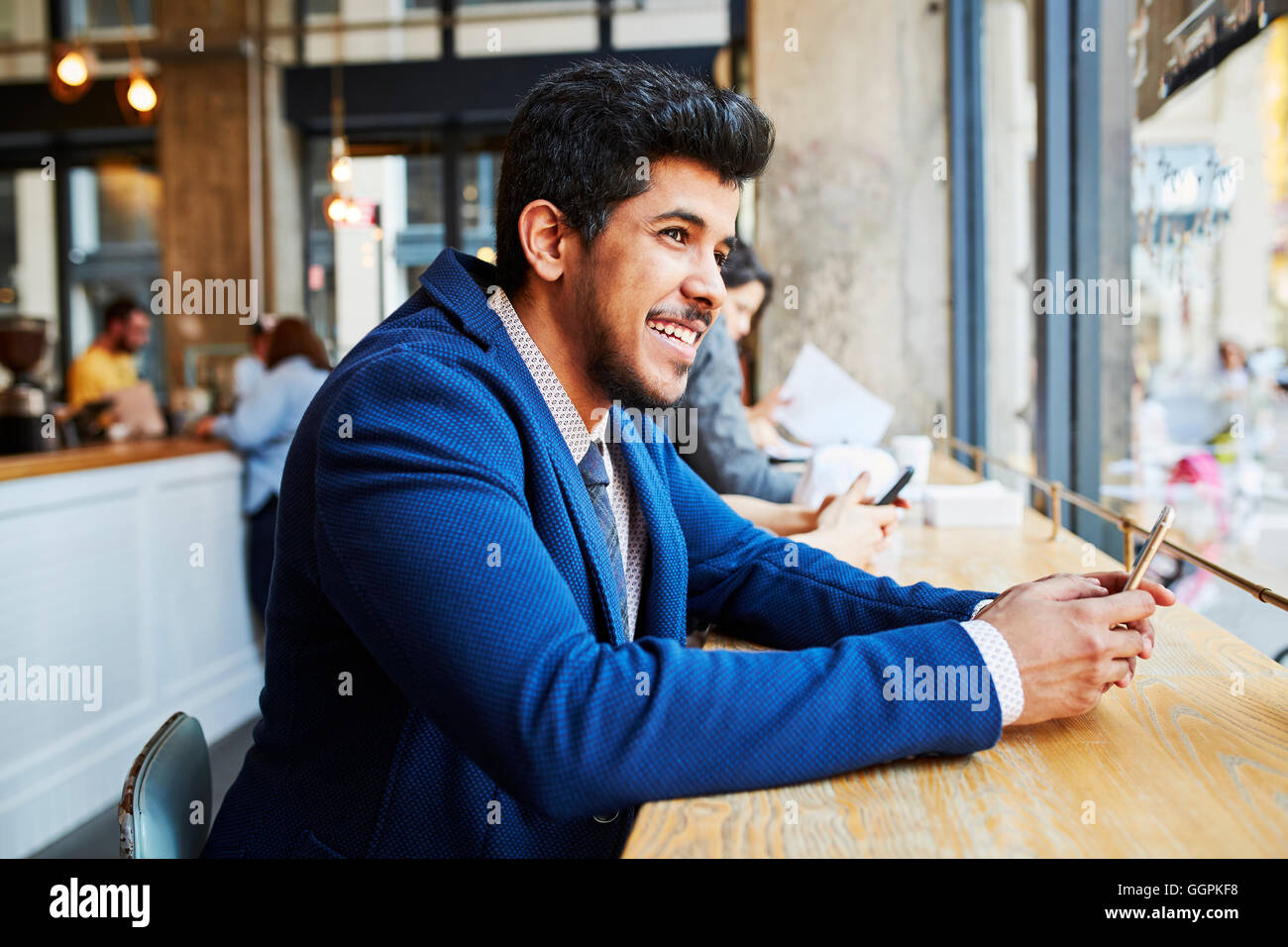 Smiling Middle Eastern man using cell phone at cafe window Stock Photo ...