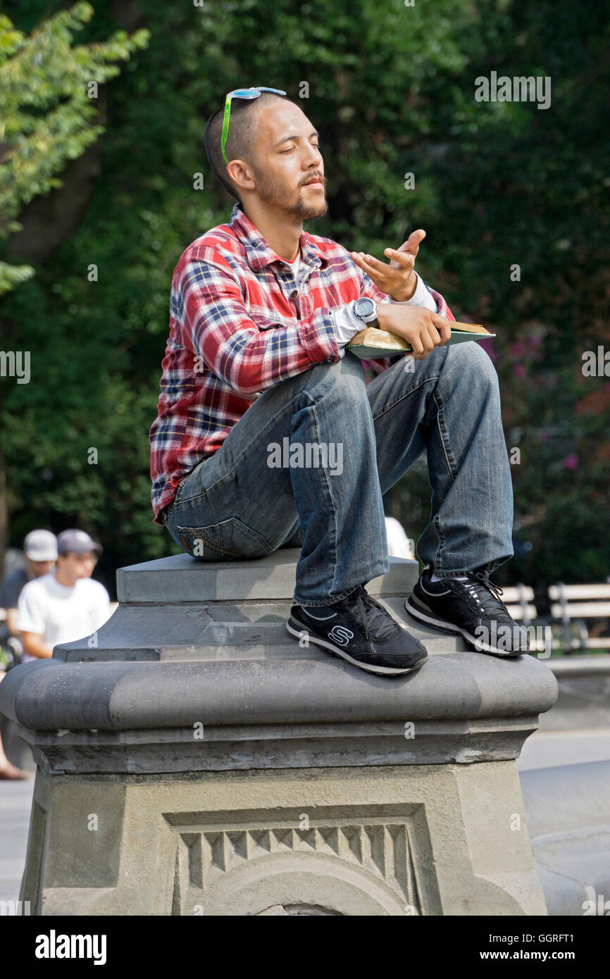 A young man pausing to meditate while sitting on a pillar and reading ...