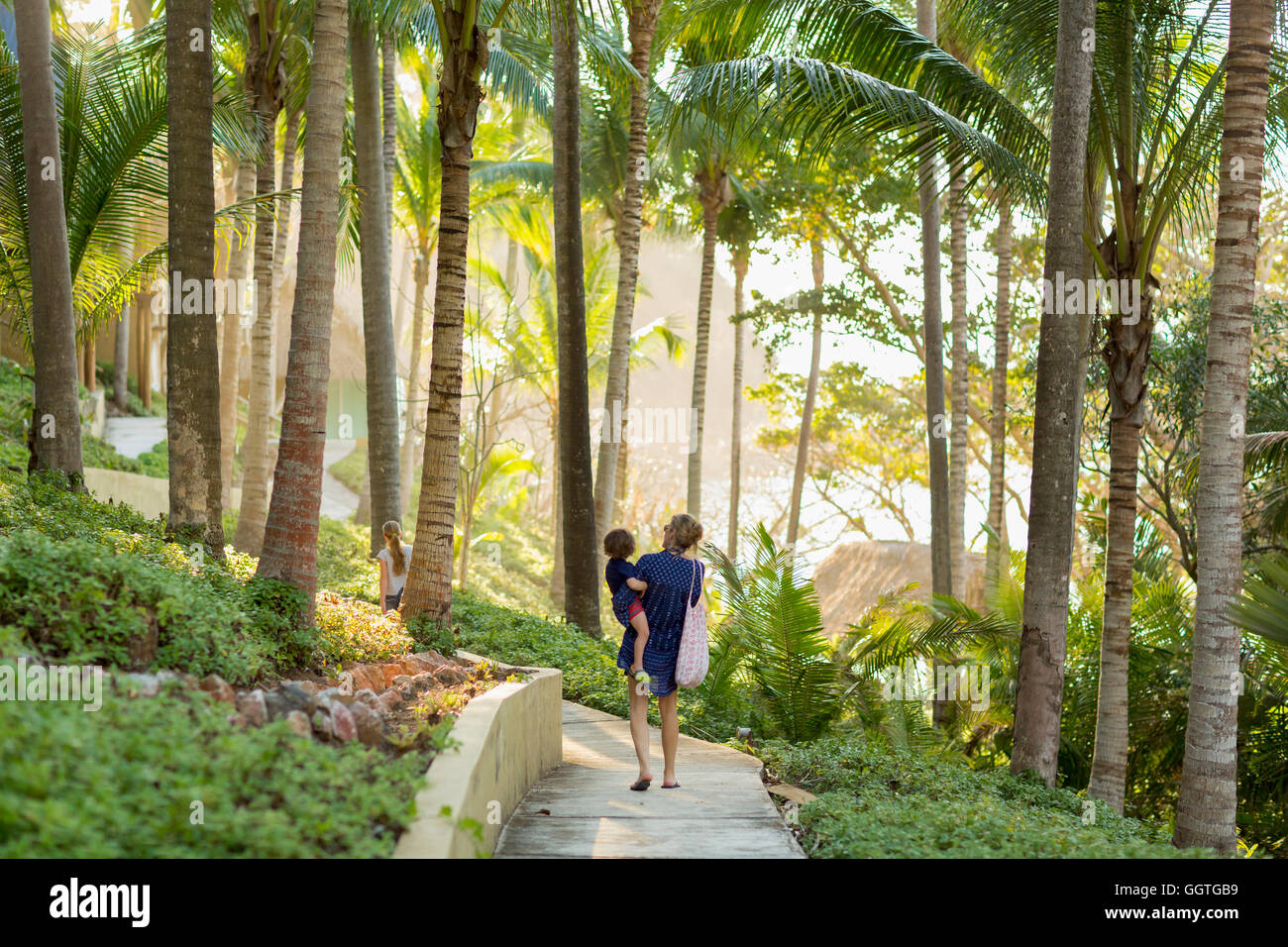 Caucasian mother carry son on path with palm trees Stock Photo - Alamy