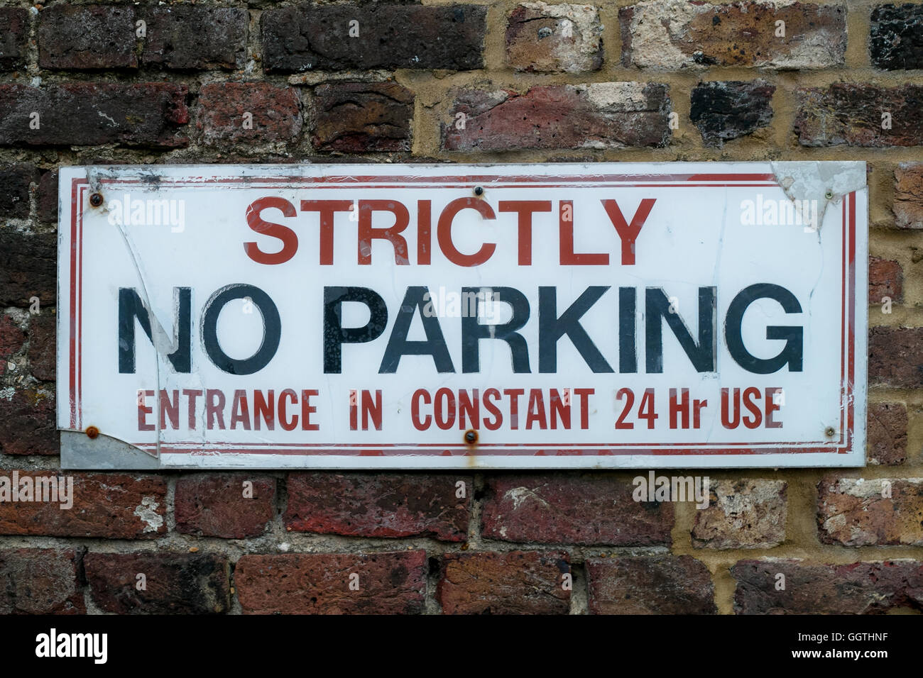 No Parking sign - chipped and slightly damaged. London brick wall in ...