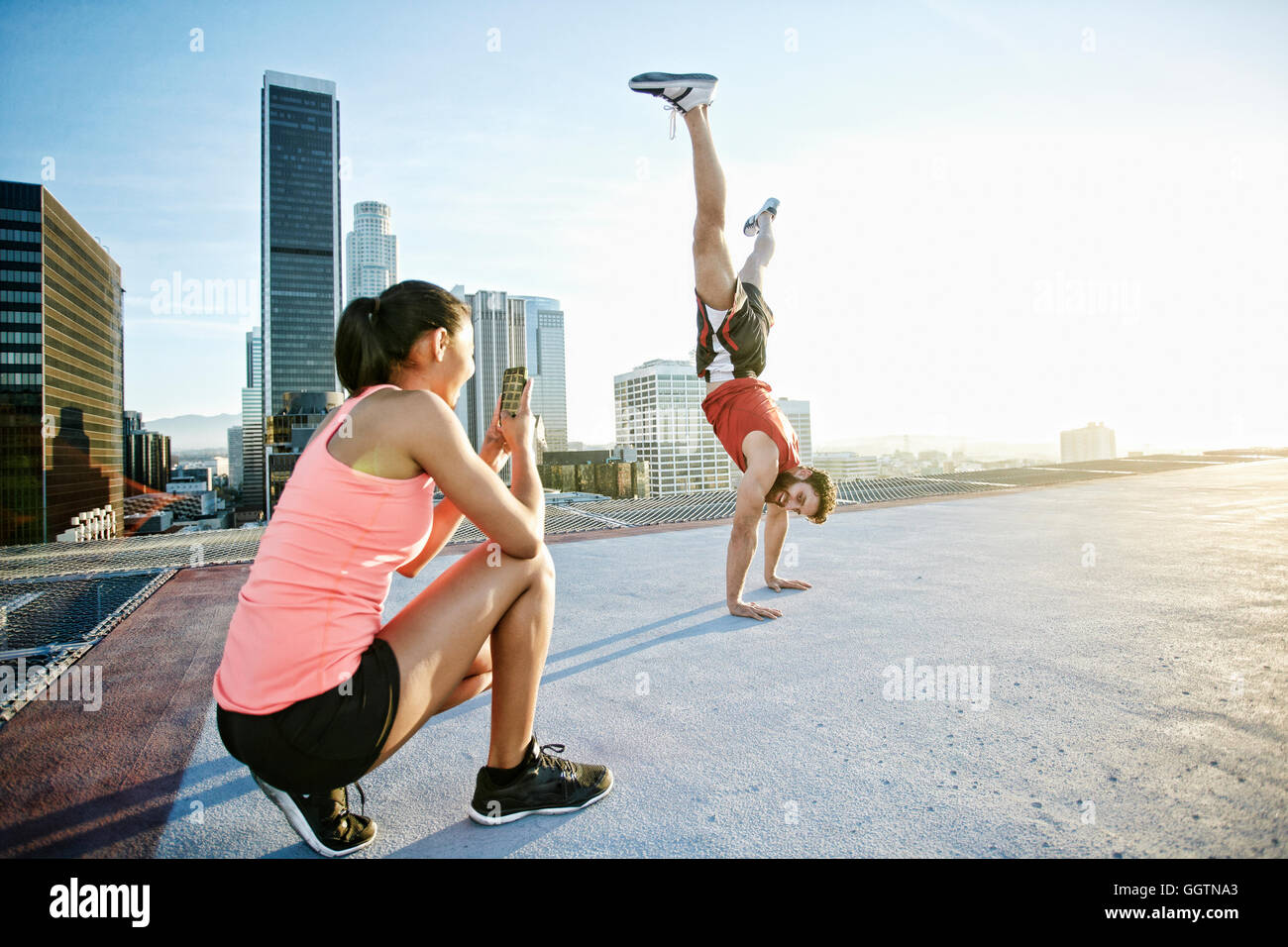 Woman photographing man doing handstand on urban rooftop Stock Photo ...
