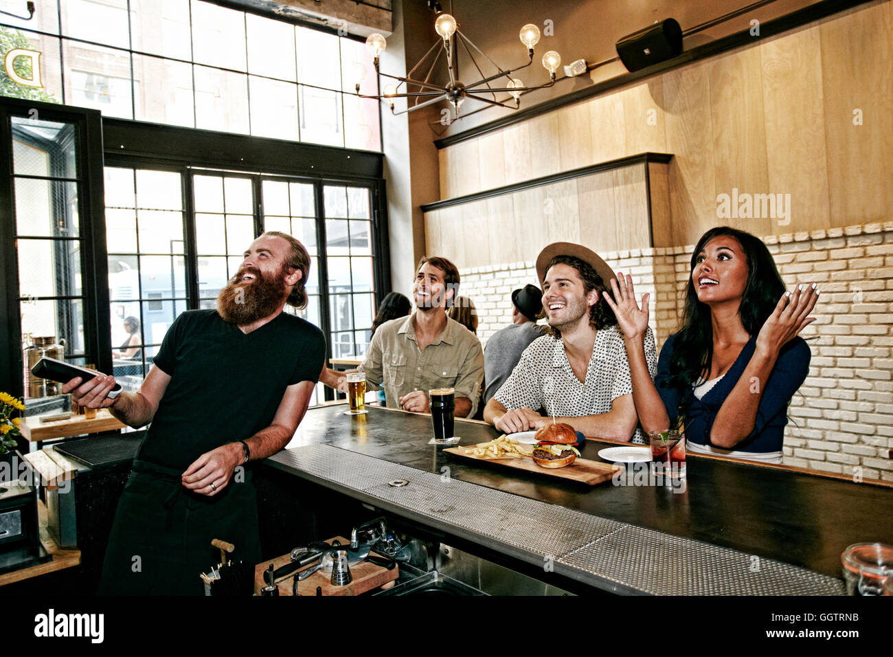 Smiling bartender and customers watching television in bar Stock Photo ...