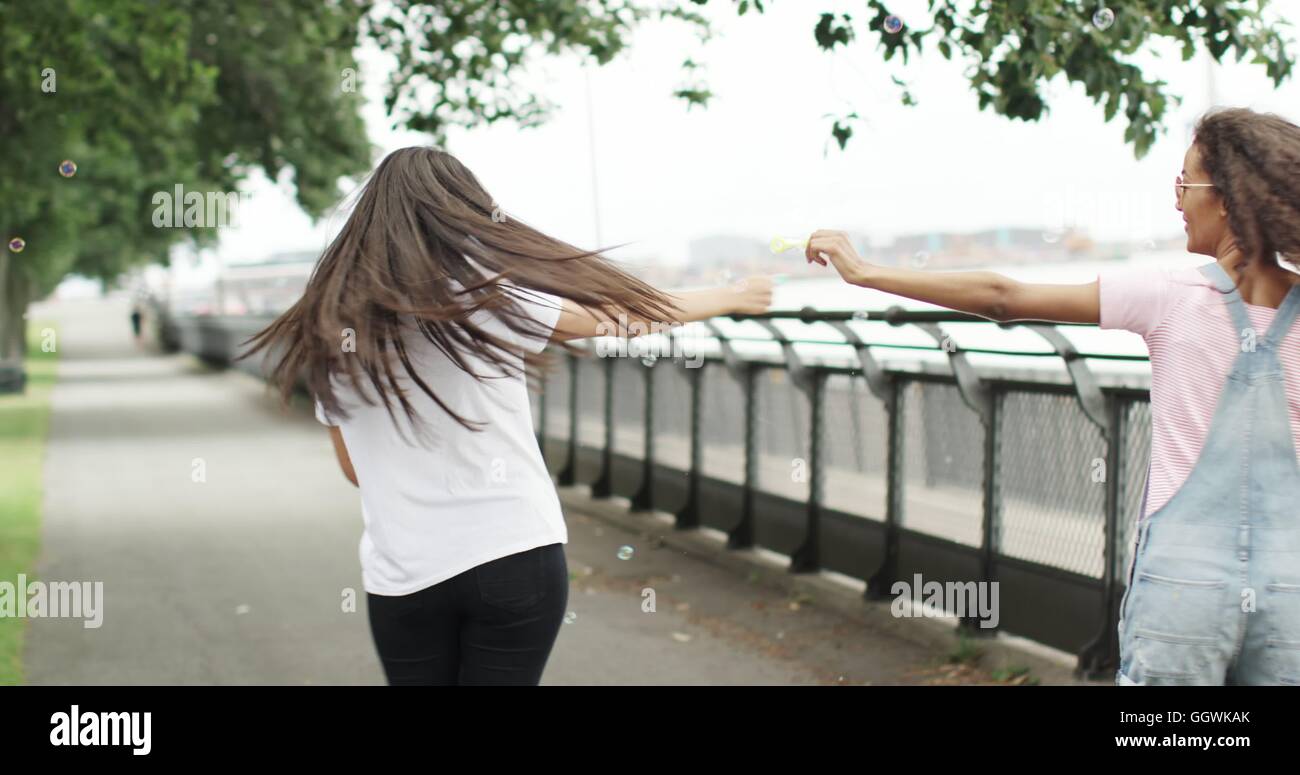 Two fun playful women making soap bubbles by twirling around on an open ...