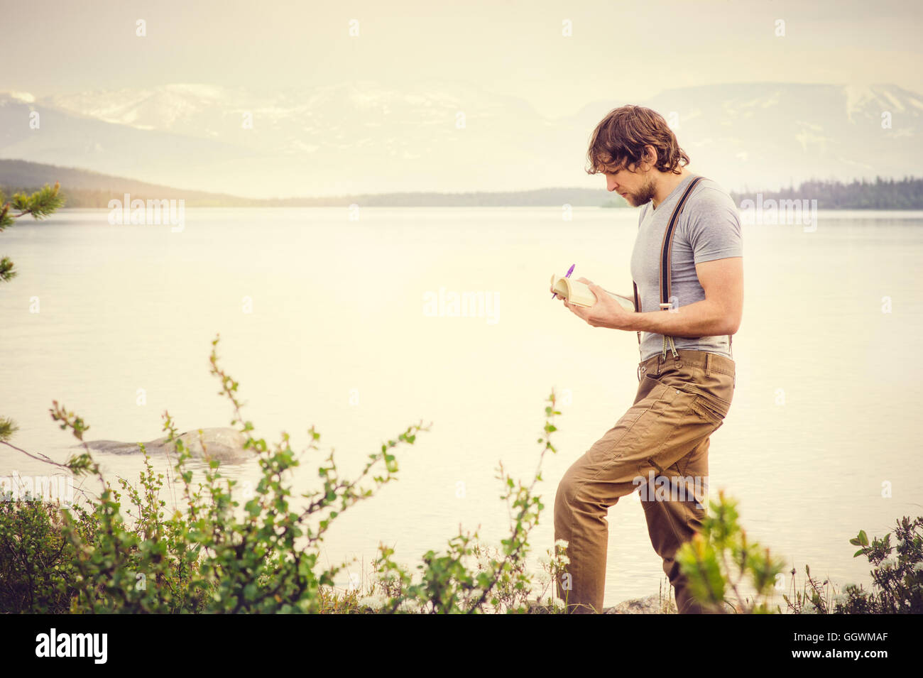 Young Man reading book and writing notes outdoor with scandinavian lake ...