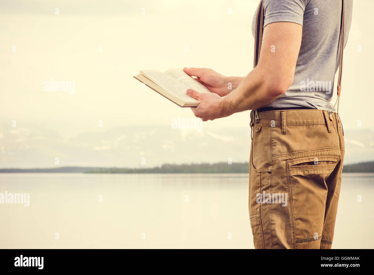 Young Man reading book outdoor with scandinavian lake and mountains on ...