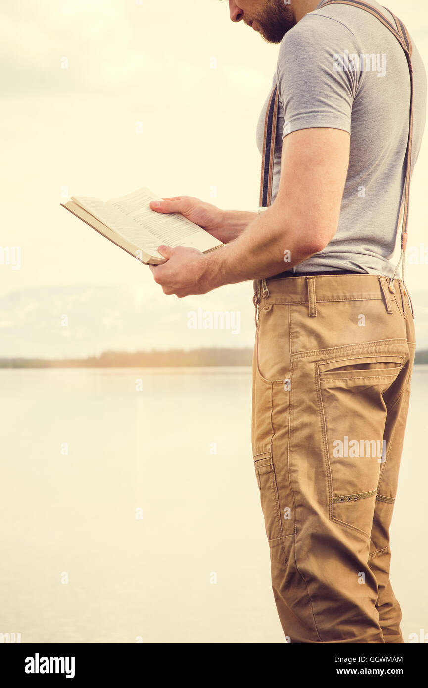 Young Man reading book outdoor with scandinavian lake and mountains on ...