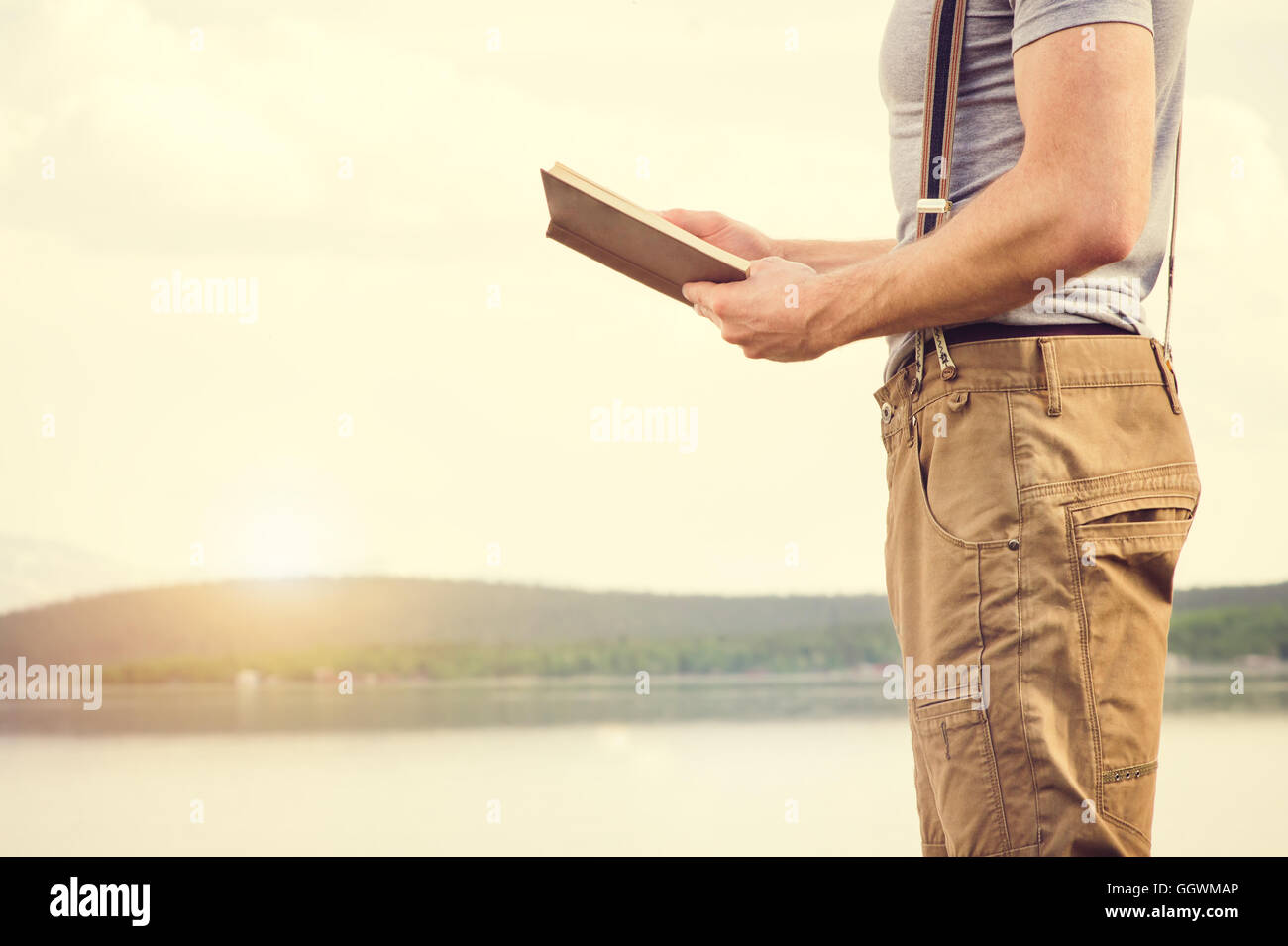 Young Man reading book outdoor with scandinavian lake and mountains on ...
