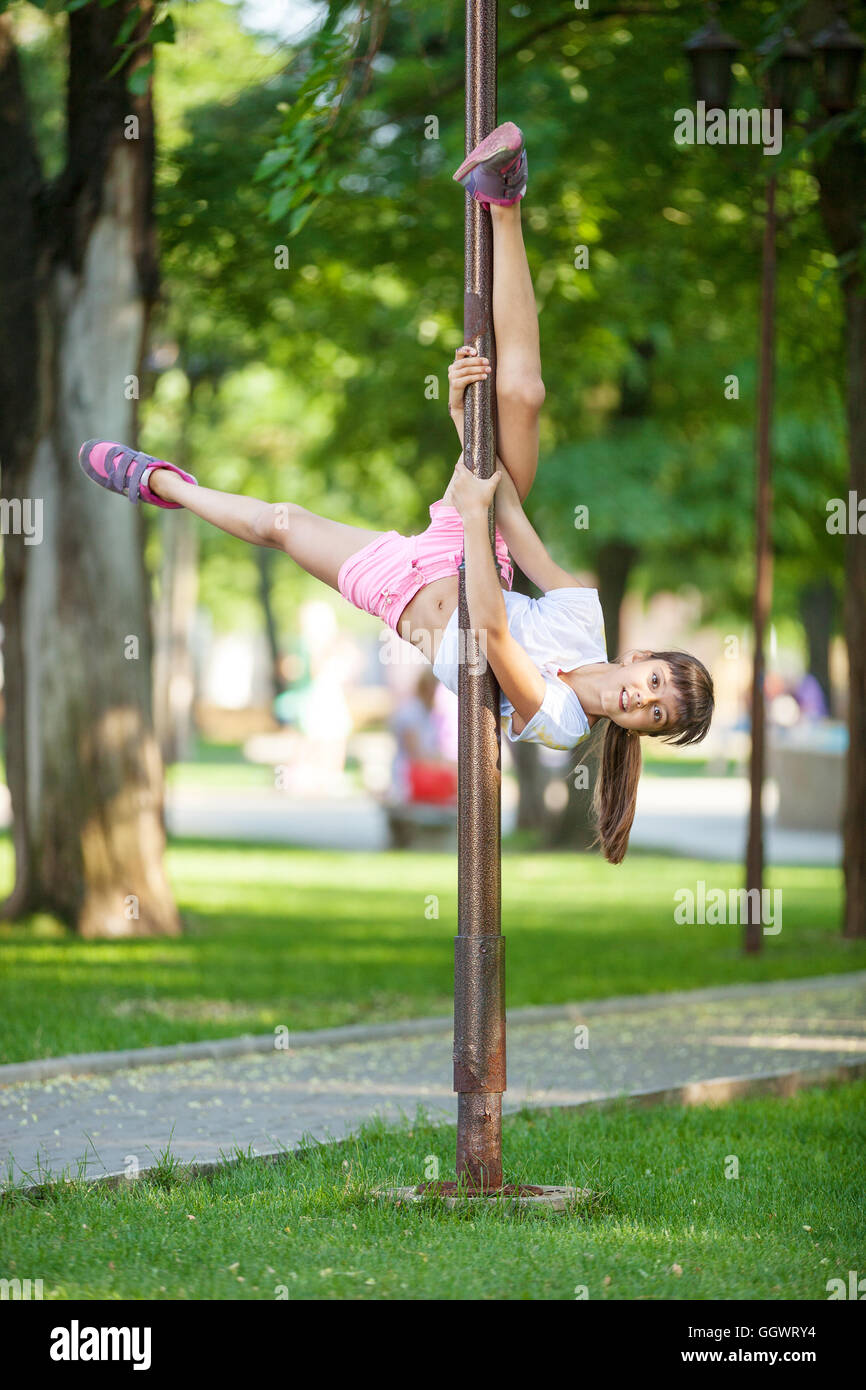 Cute girl having fun outdoor using a street lamp as a gymnastic pole ...