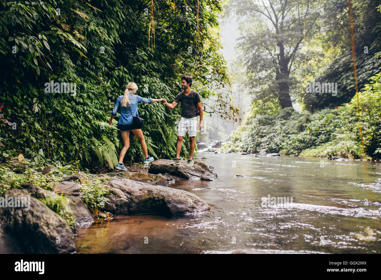 Couple climbing on rocks by mountain stream. Outdoor shot of young man ...
