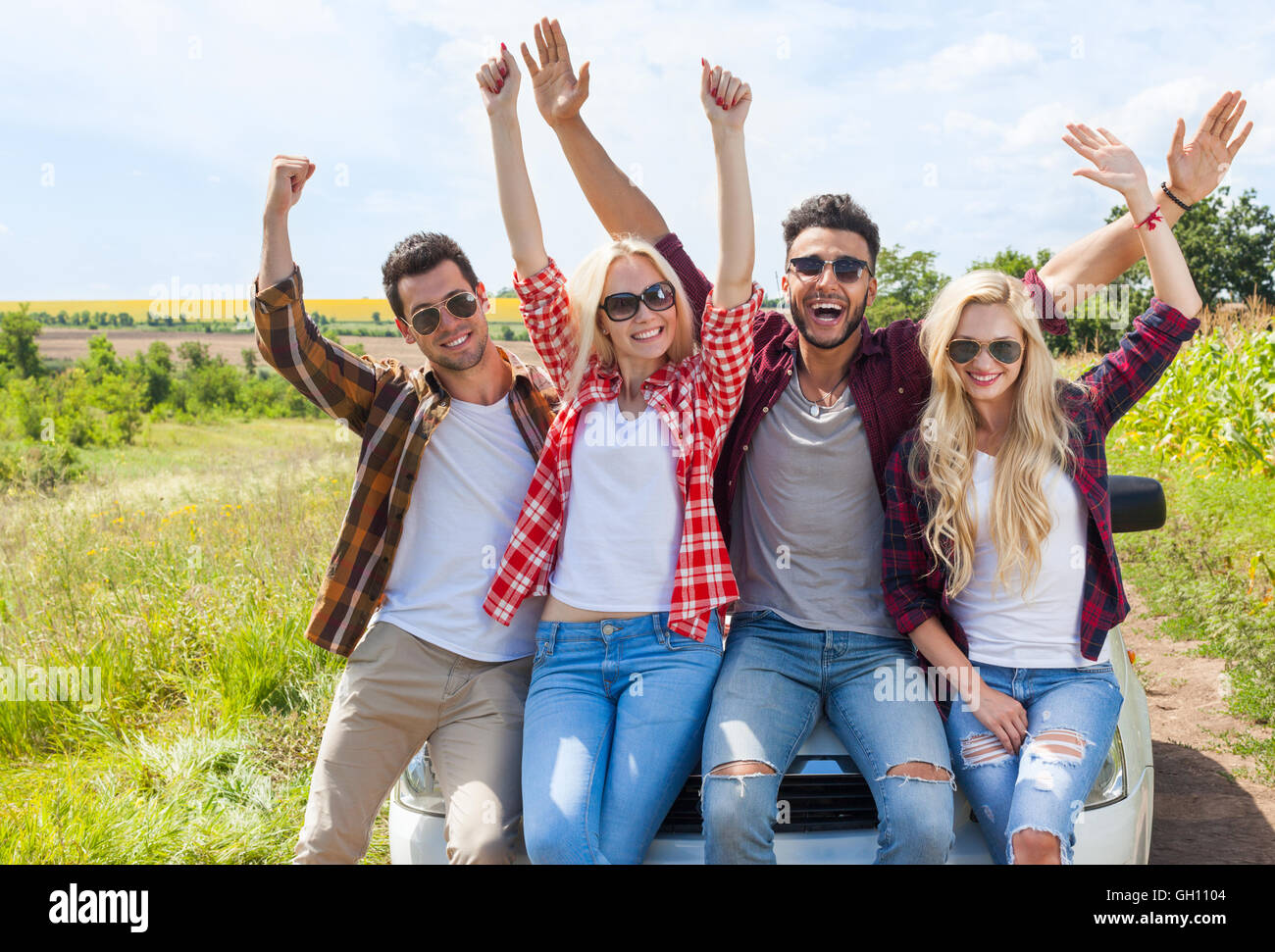 Excited friends on car outdoor countryside raise arms people smile ...