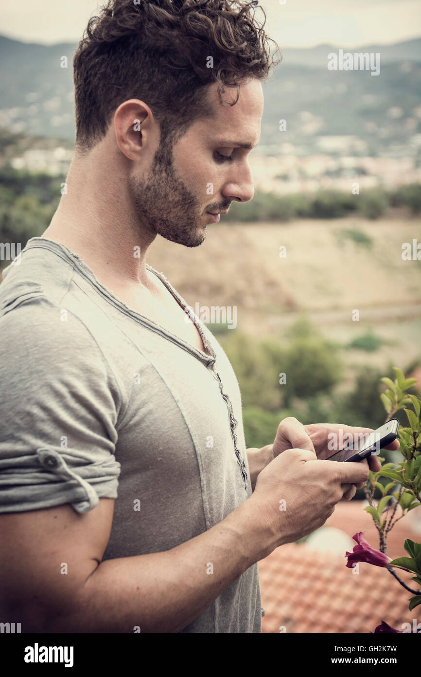 Handsome trendy man using cell phone to type text message outdoor. Side ...