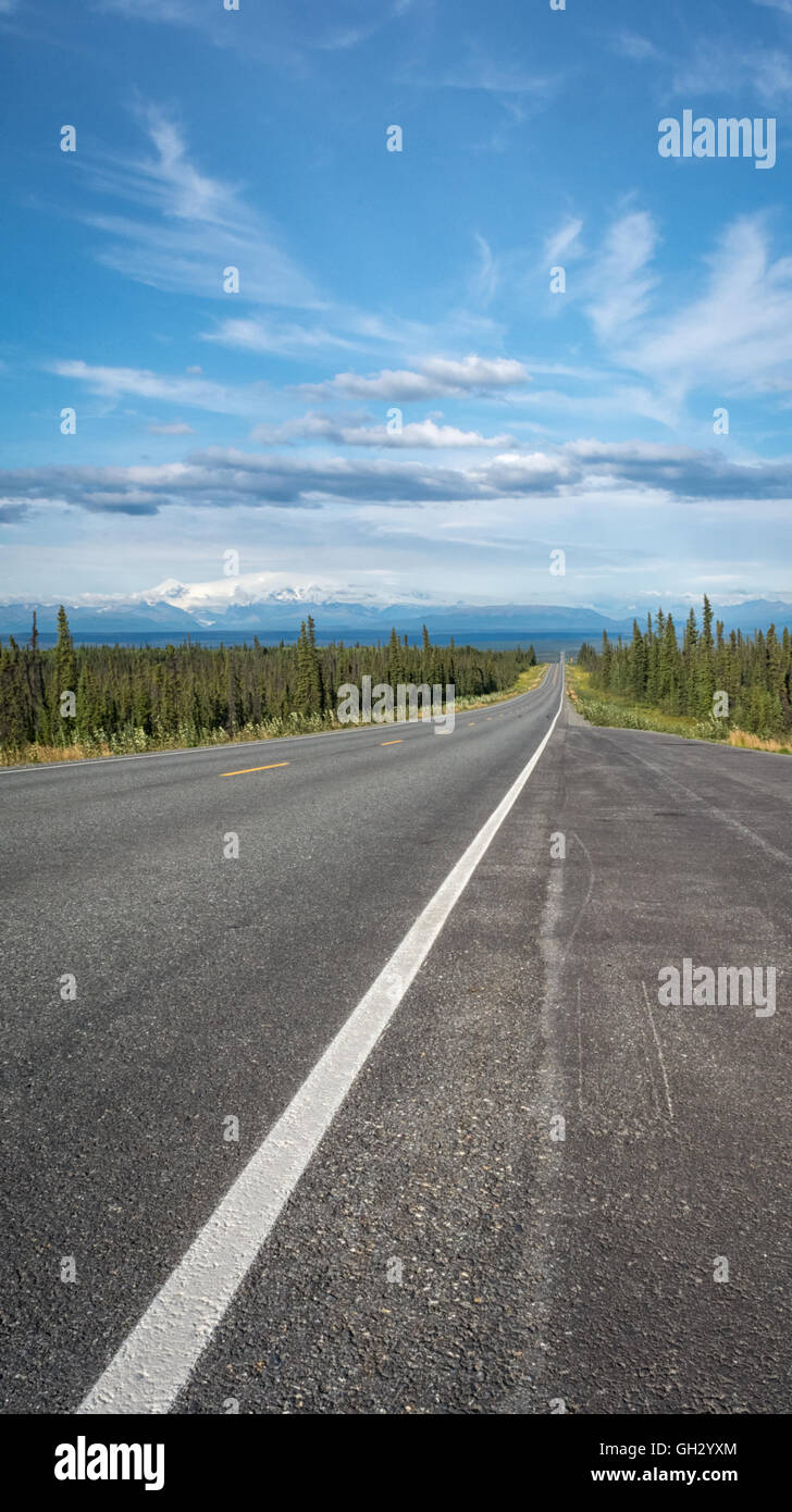 A two lane highway stretches towards distant snow capped mountain in ...
