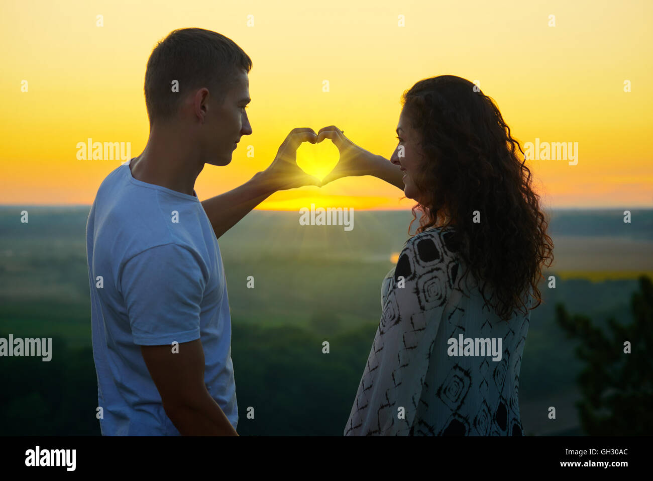 romantic couple at sunset make a heart shape from hands, the rays of ...