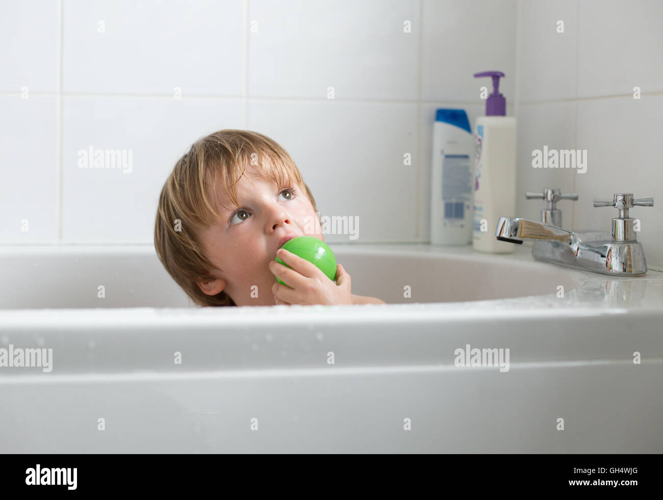 young boy in bath shampoo eating plastic apple thoughtfully looking up ...