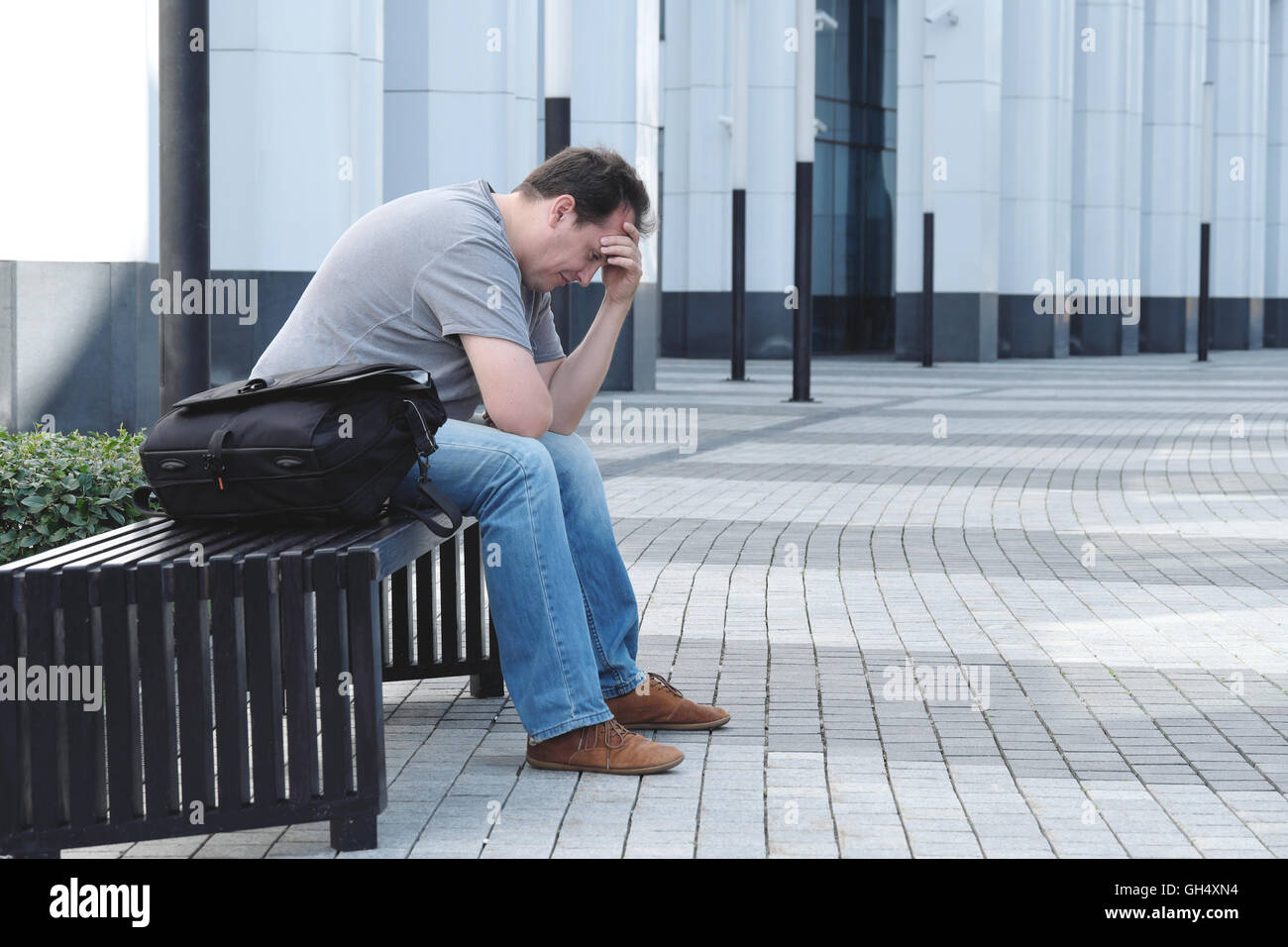 Sad man sitting in front of white office building Stock Photo - Alamy