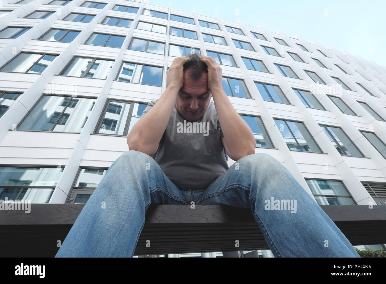 Sad man sitting in front of white office building Stock Photo - Alamy