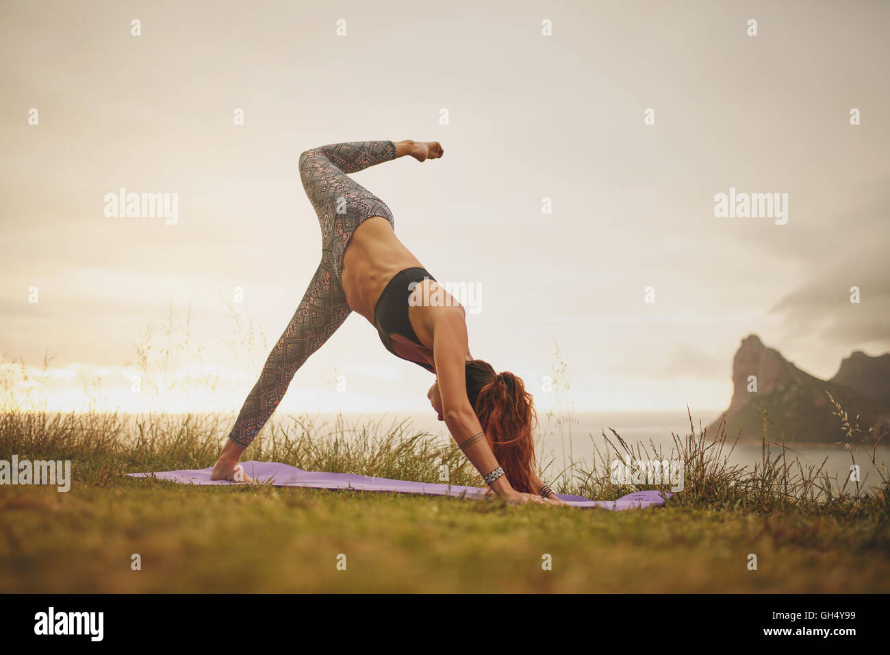 Side view shot of young woman practicing yoga outdoors on cliff ...