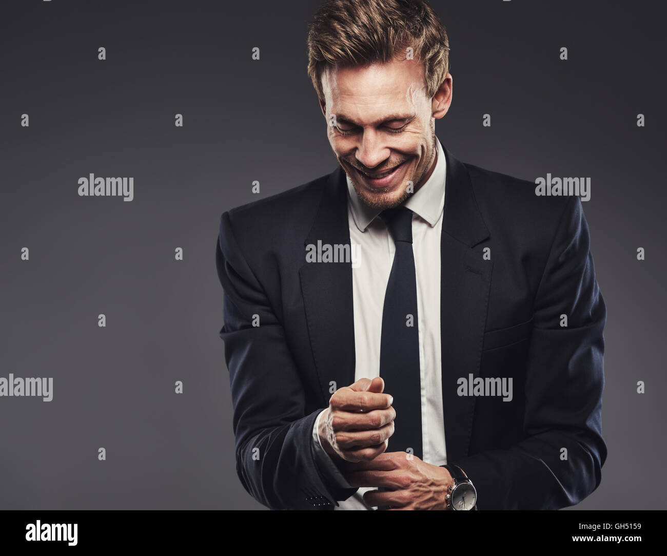 Handsome young man in a black suit adjusting his jacket cuff, standing ...
