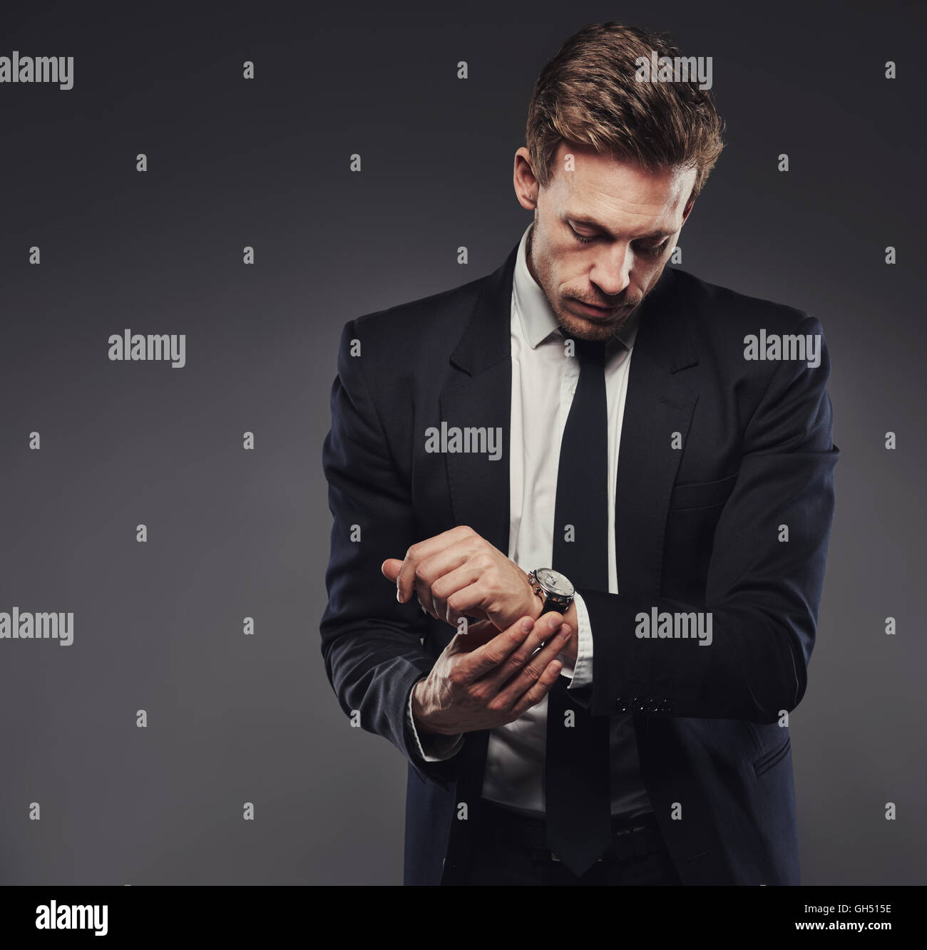 Handsome young businessman in a black suit checking the time on his ...