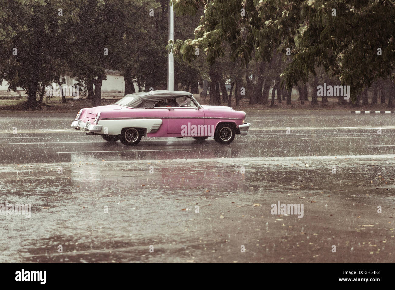 Pink American convertible classic car driving in heavy summer rain in ...