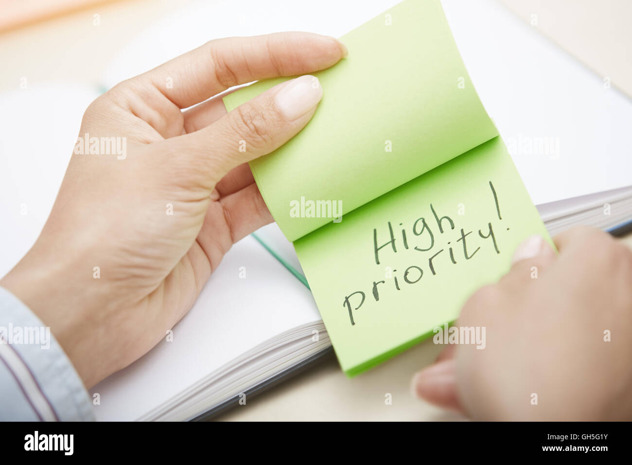Hands of businessperson holding adhesive note with High priority text ...