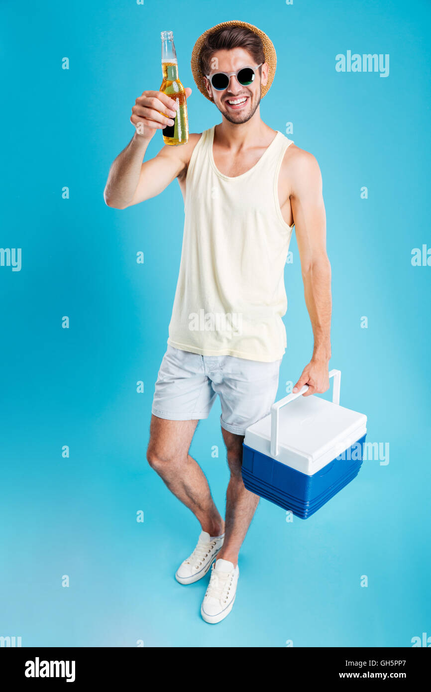 Full length of smiling young man holding cooler bag and drinking beer ...