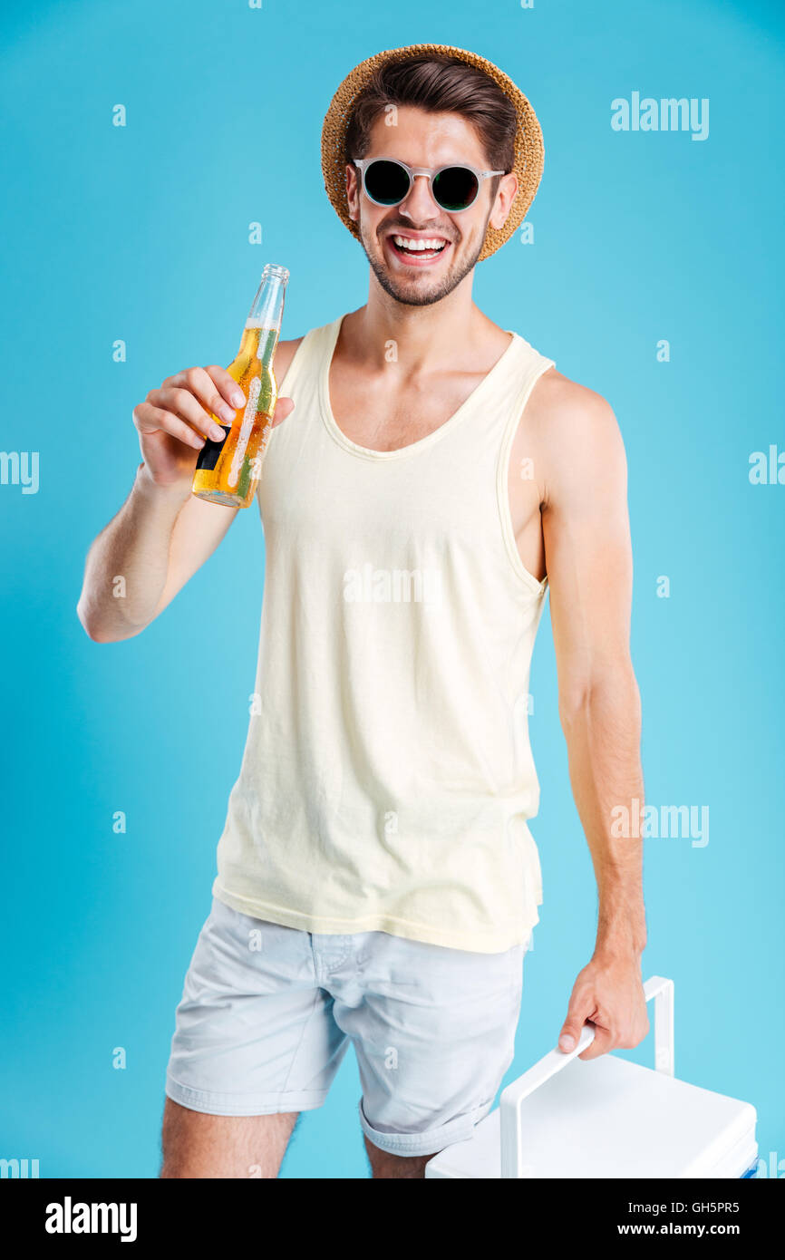 Happy handsome young man with cooler bag standing and drinking beer ...