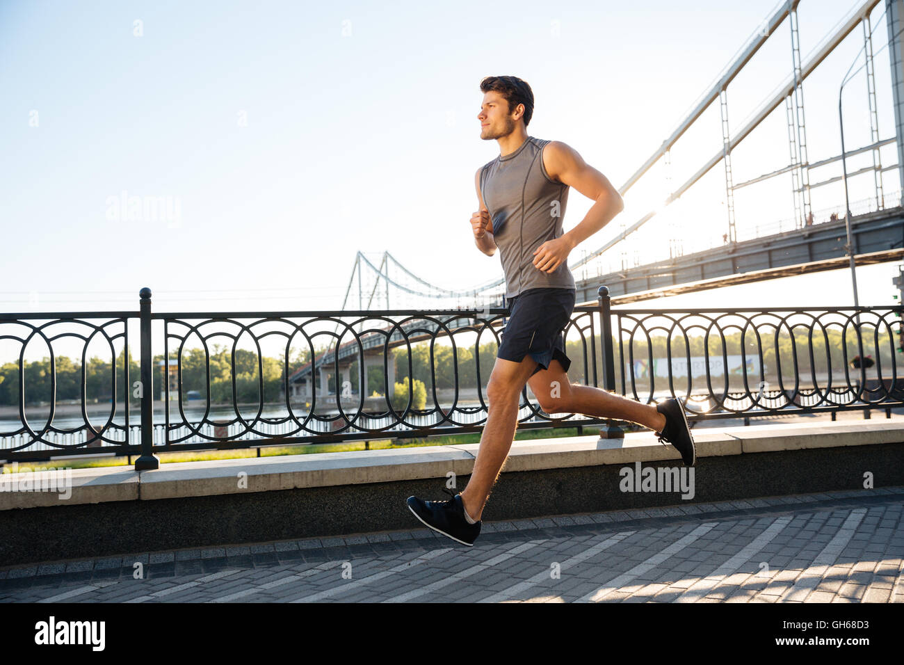 Side view of a handsome sports man running fast along big modern bridge ...
