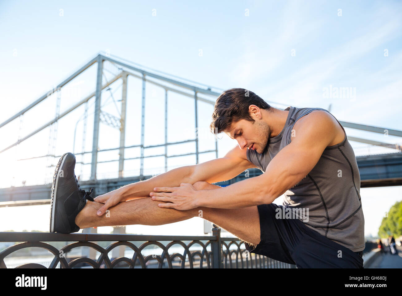 Handsome young sports man doing stretching leaning against bridge ...