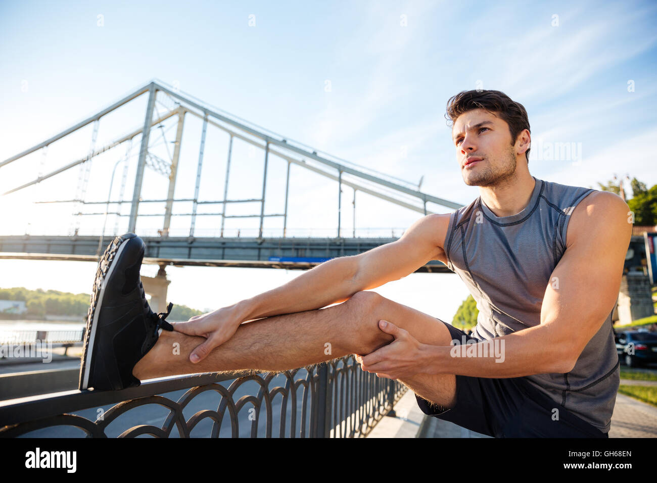 Handsome young sports man doing stretching leaning against bridge ...