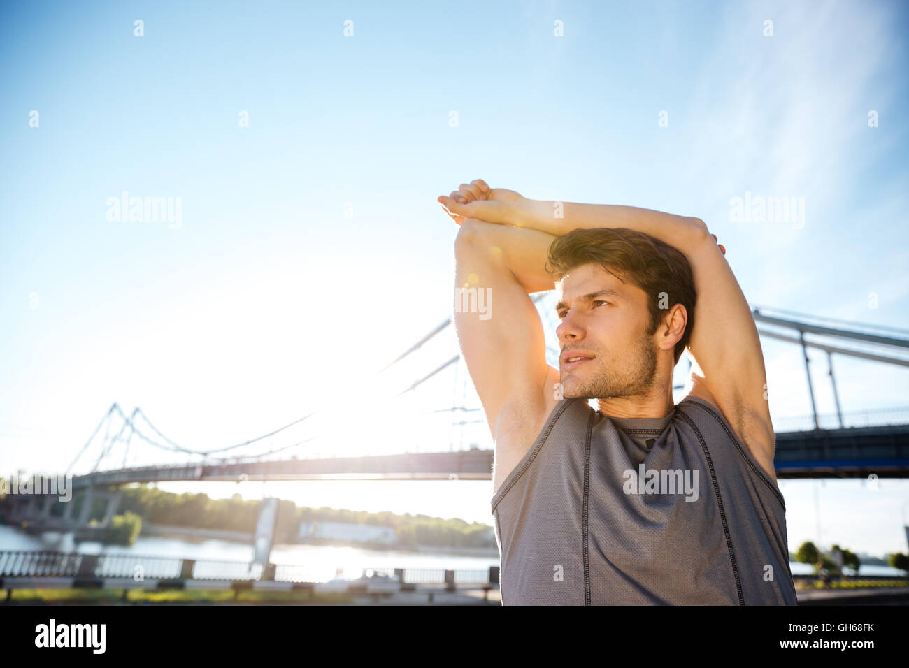 Handsome young sports man doing stretching at the bridge railing and ...