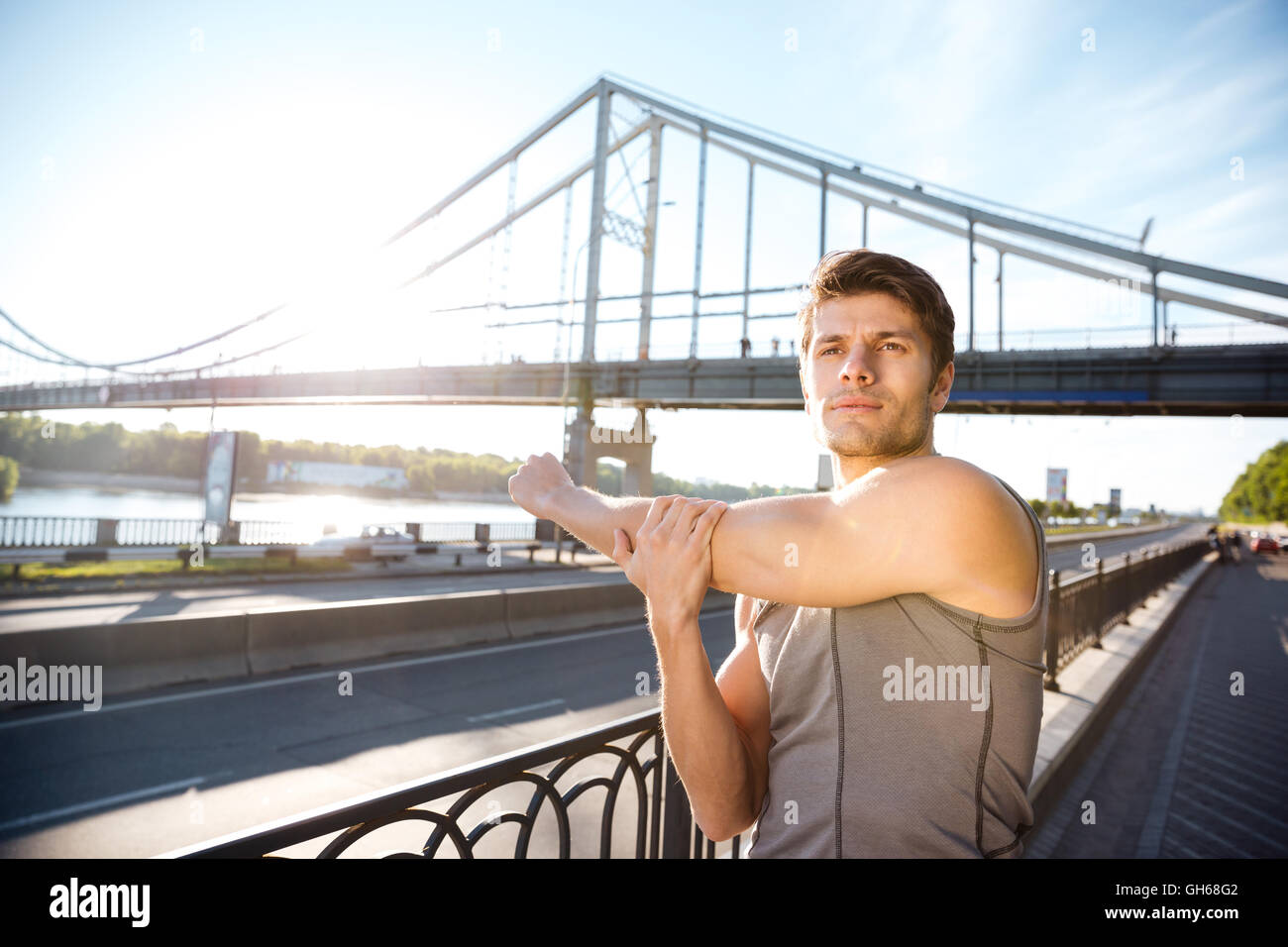 Handsome young sports man doing stretching at the bridge railing and ...
