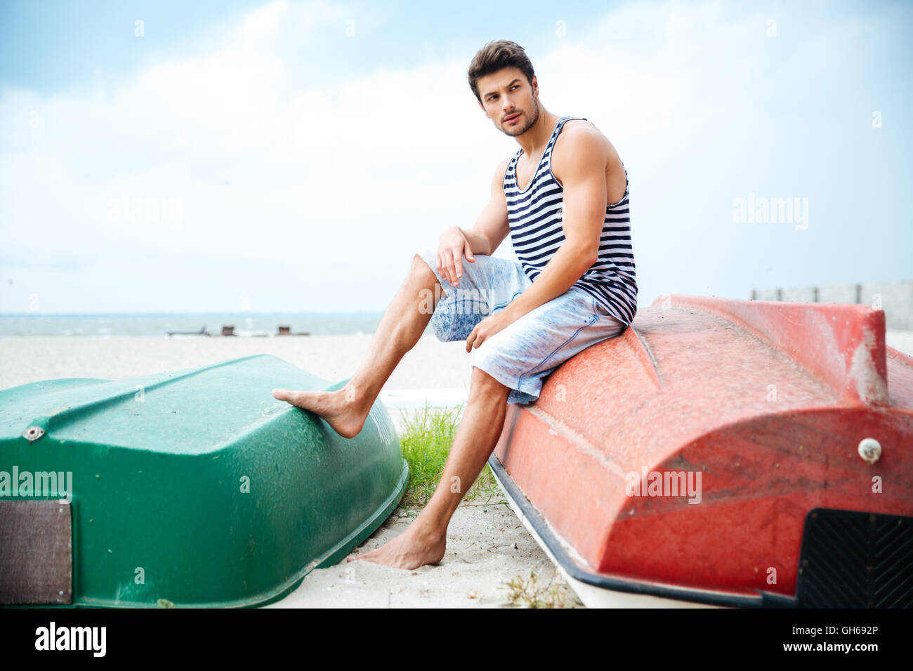 Handsome young man sitting on a fishing boat and looking away by the ...