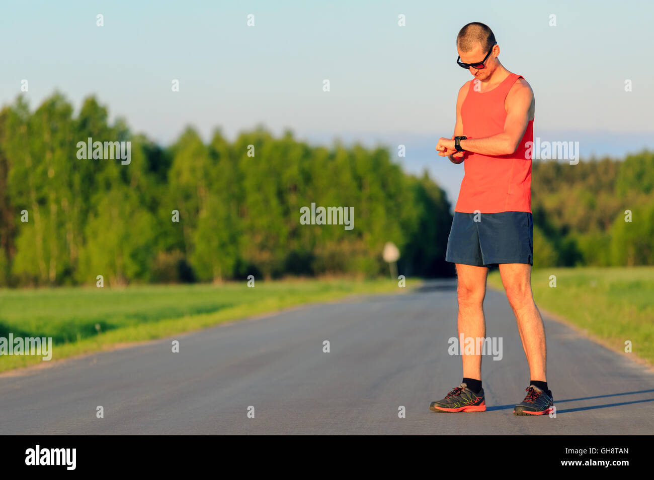 Man runner running on country road in summer sunset. Checking sports ...