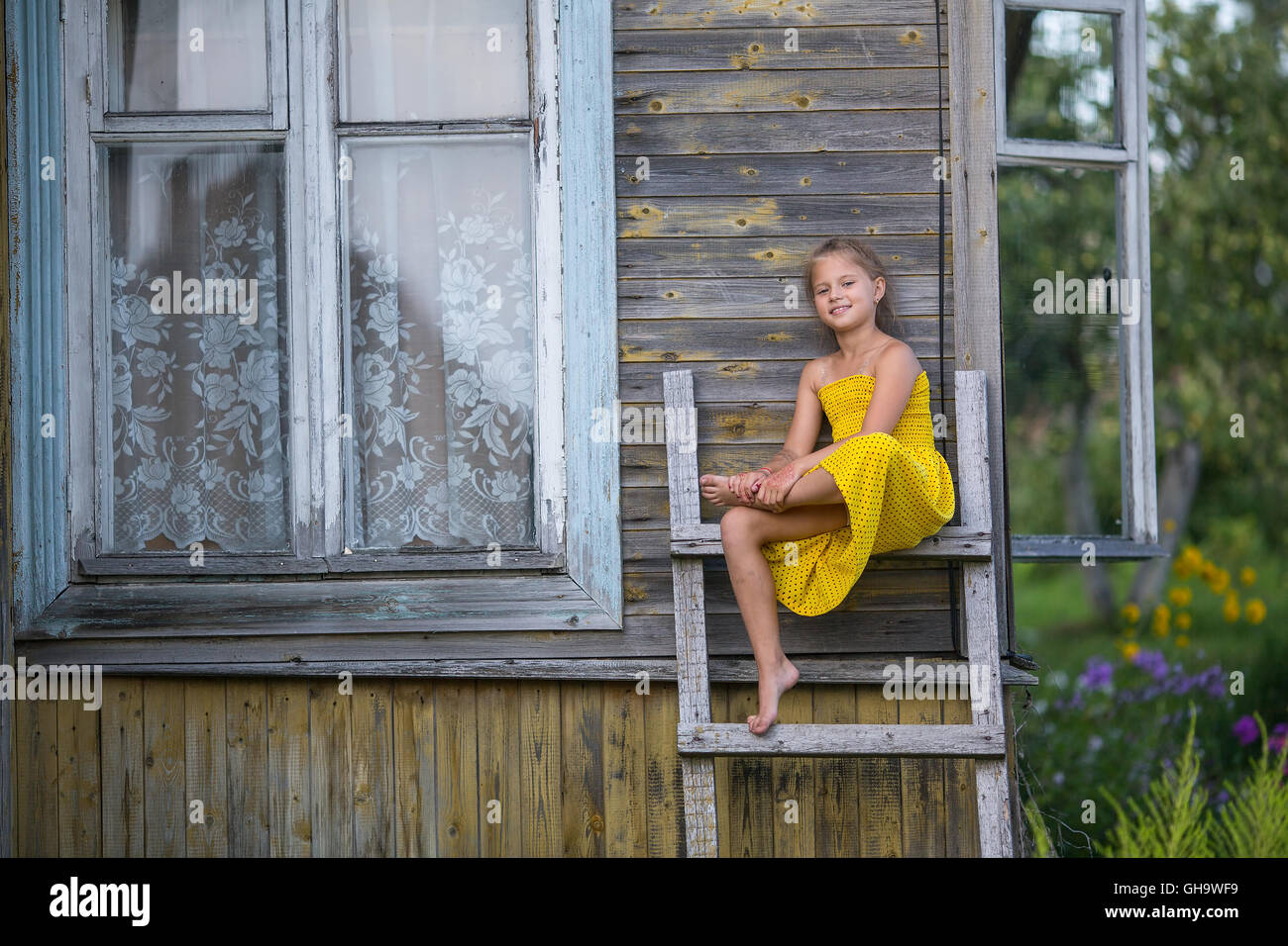 Little cute girl sitting on a wooden ladder near a village house Stock ...